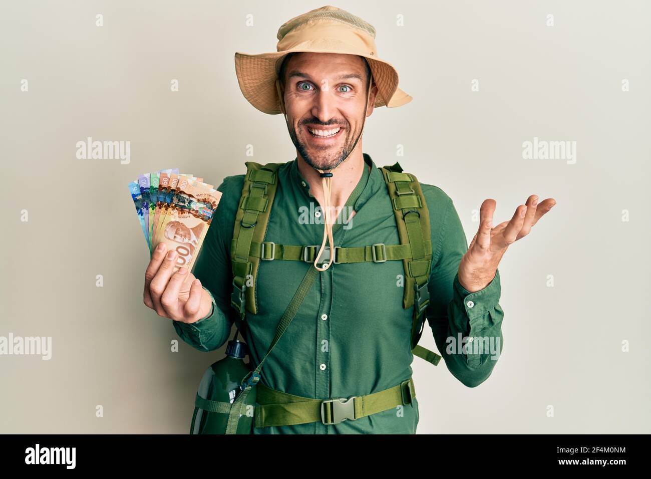 Handsome man with beard wearing explorer hat holding canadian dollars ...