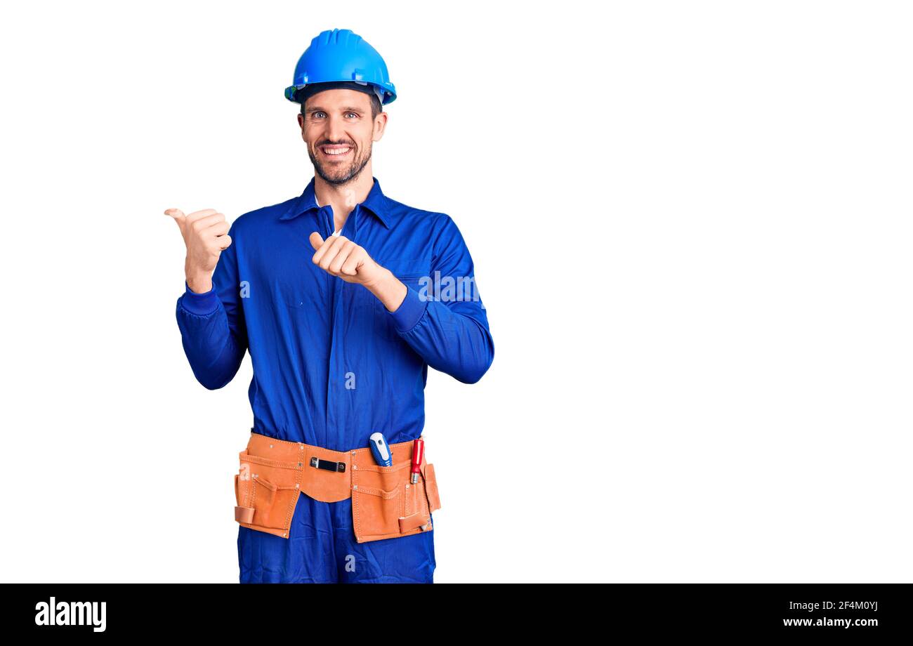 Young handsome man wearing worker uniform and hardhat pointing to the ...