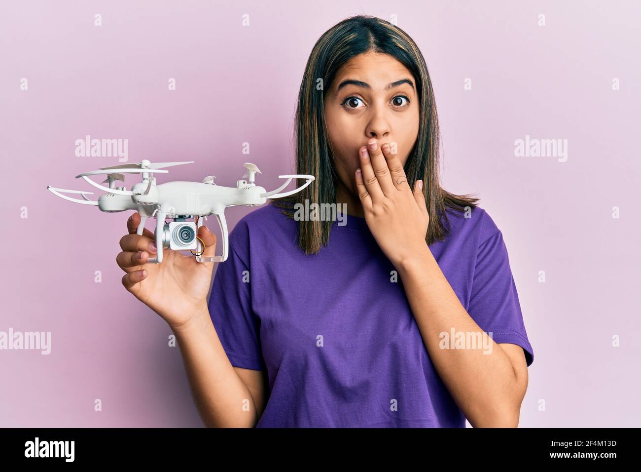 Young latin woman using drone covering mouth with hand, shocked and ...