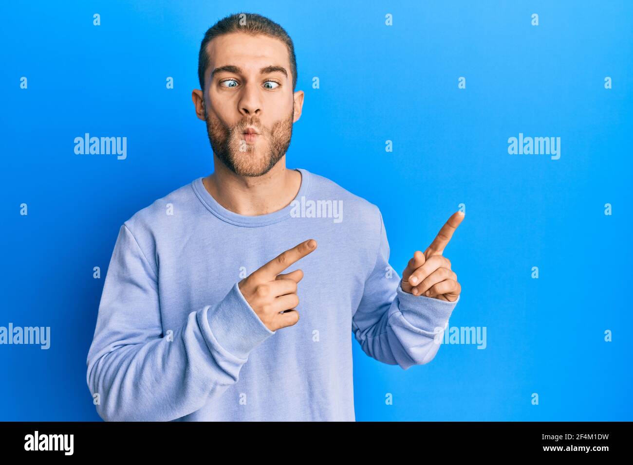 Young caucasian man pointing with fingers to the side making fish face ...