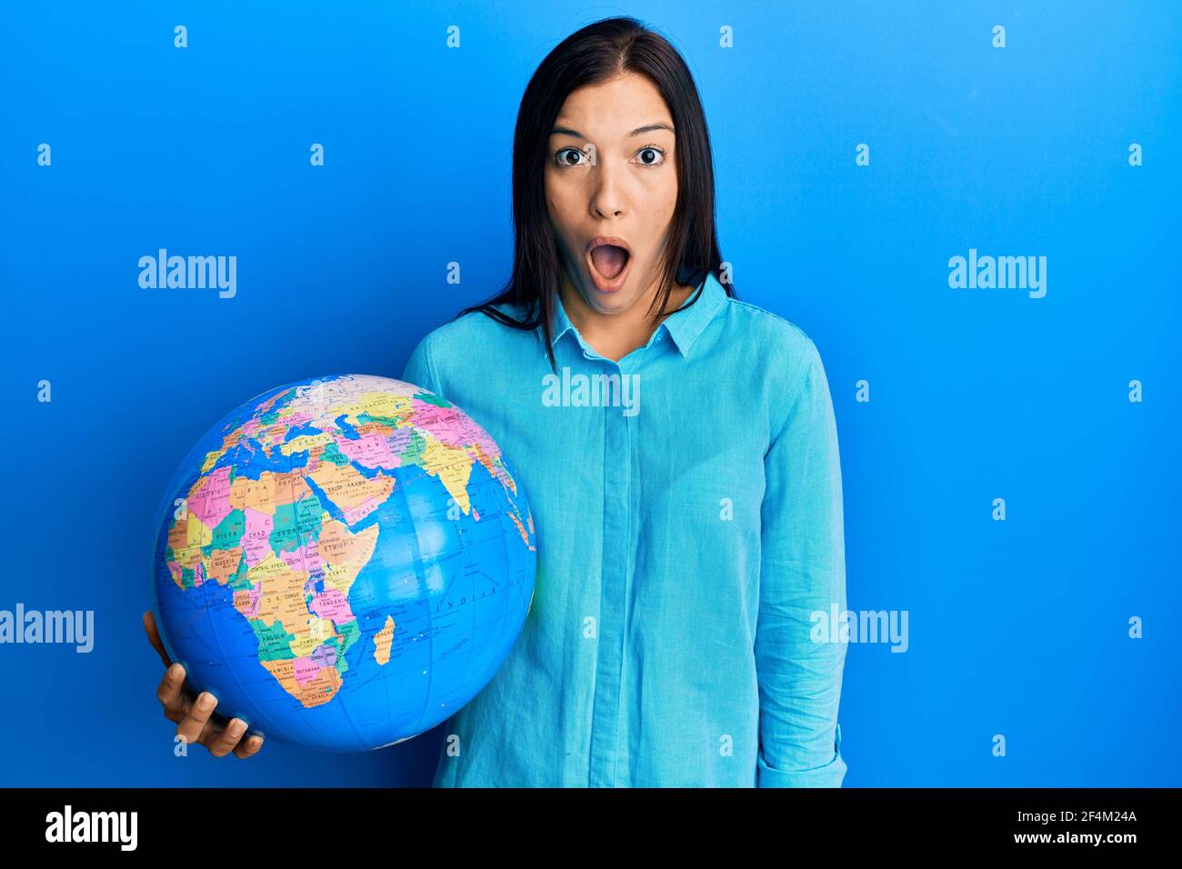 Young latin woman holding big world ball scared and amazed with open ...