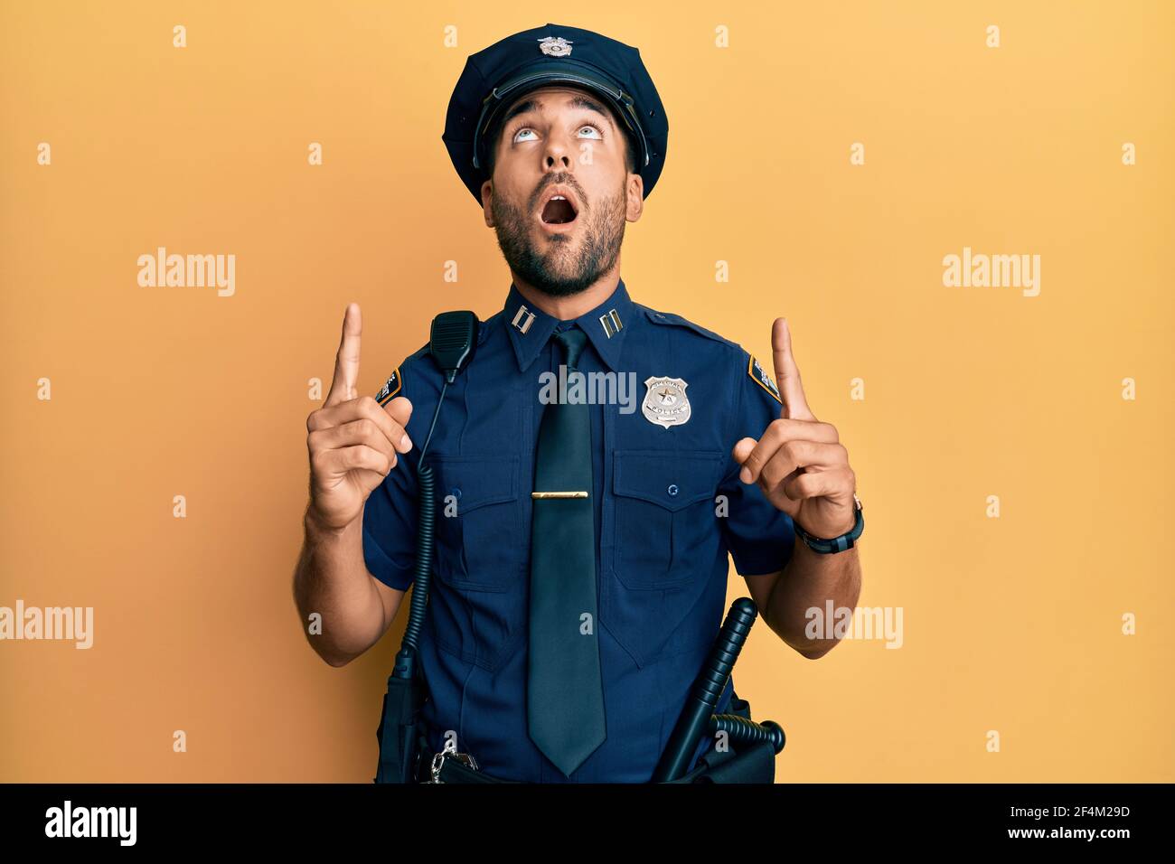 Handsome hispanic man wearing police uniform amazed and surprised ...
