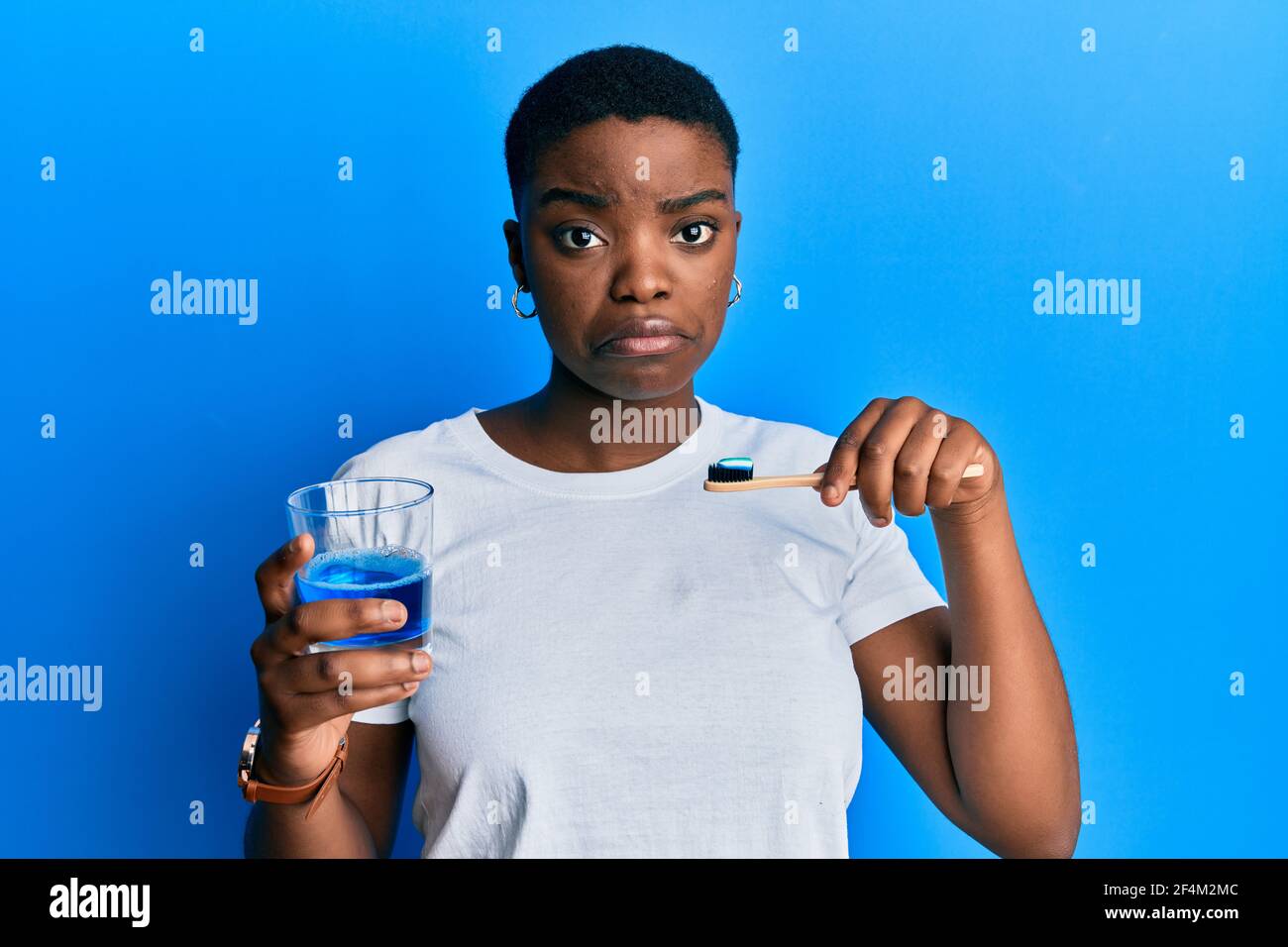 Young african american woman holding glass of mouthwash and toothbrush ...