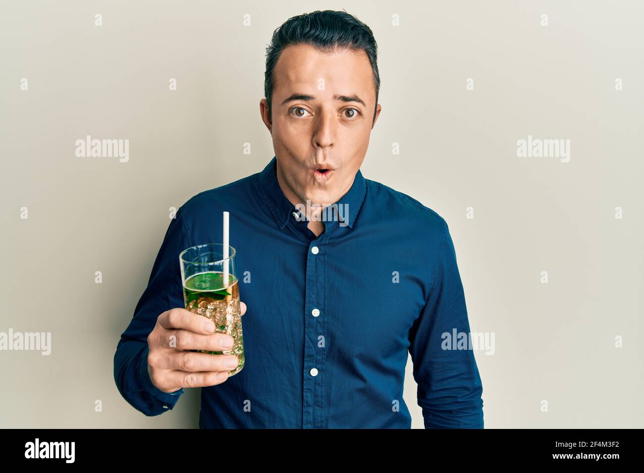 Handsome young man drinking mojito glass scared and amazed with open ...