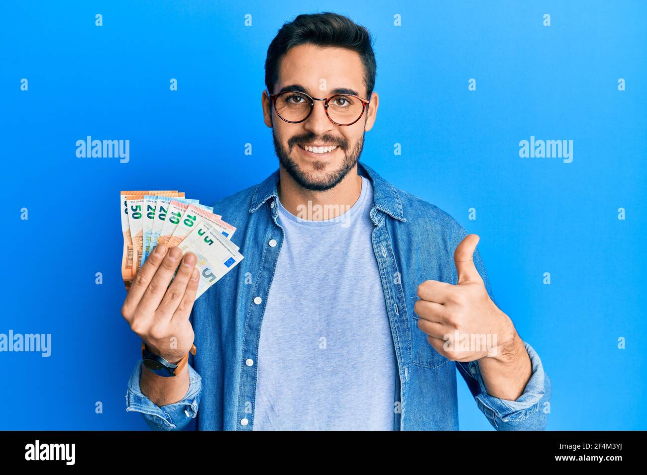 Young hispanic man holding euro banknotes smiling happy and positive ...