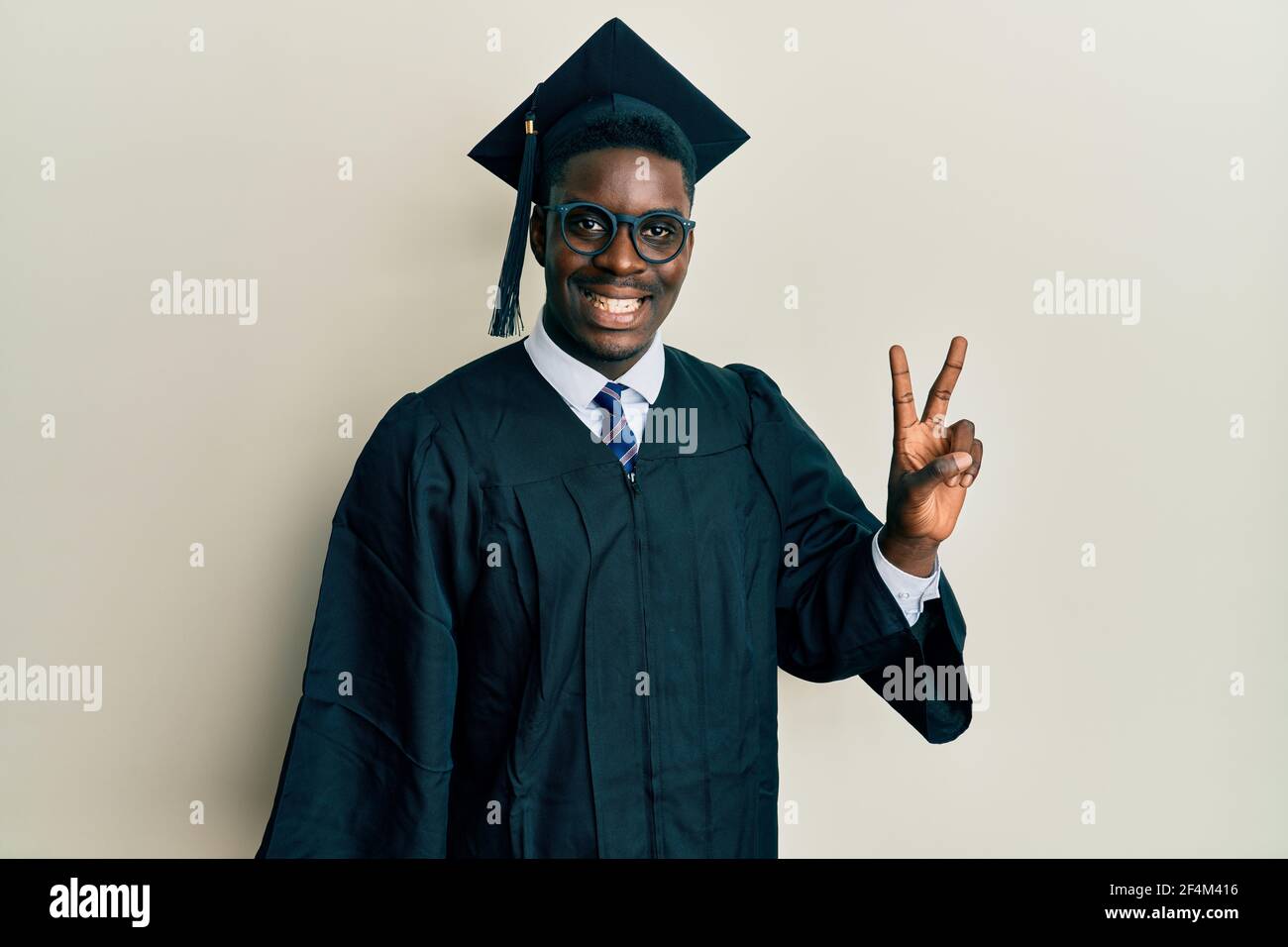 Handsome black man wearing graduation cap and ceremony robe smiling ...