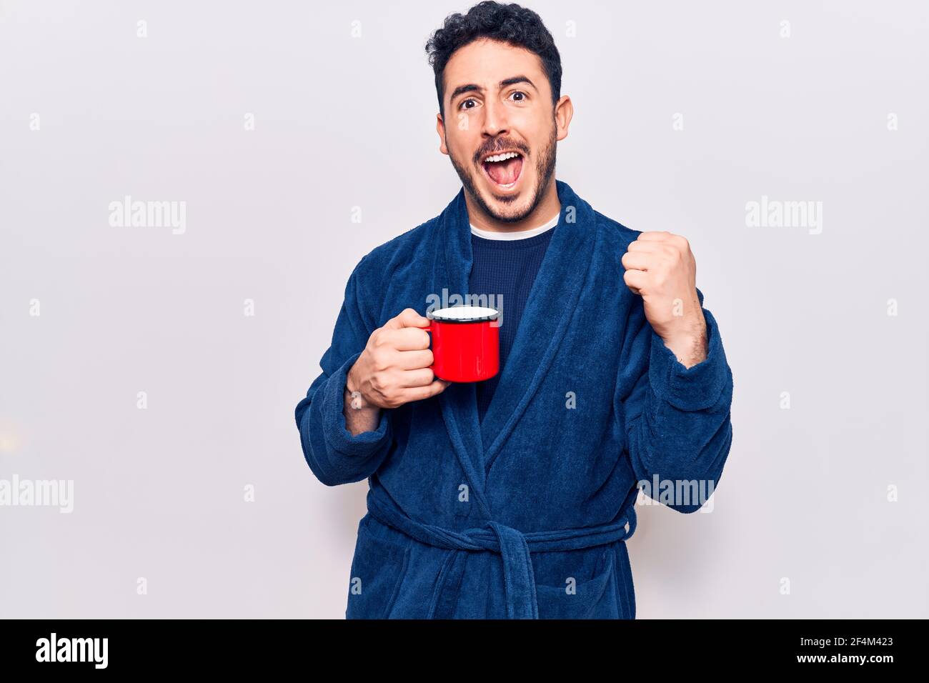Young hispanic man wearing robe holding coffee screaming proud ...