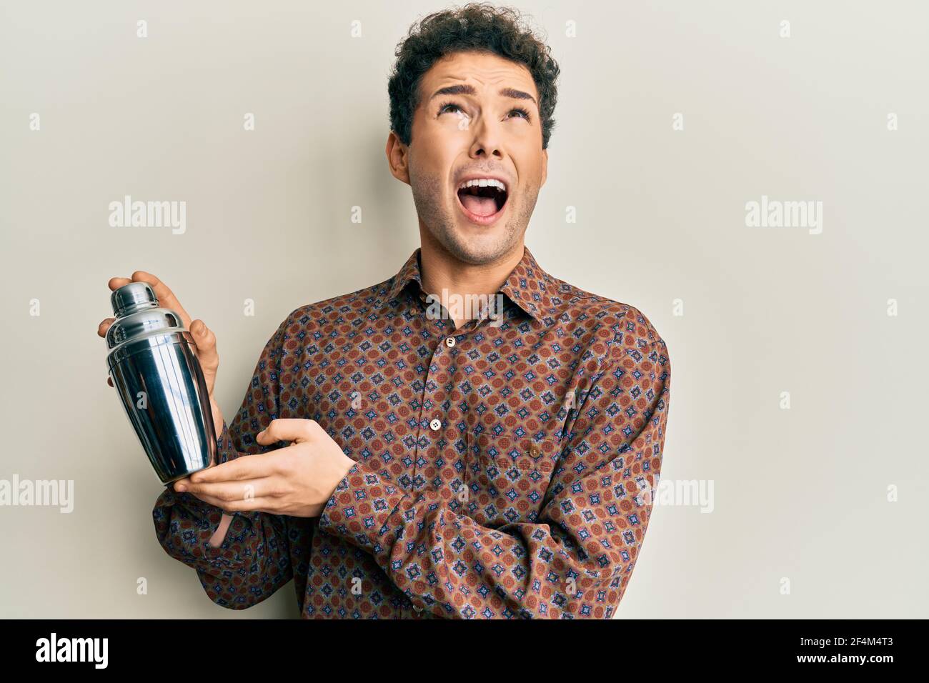 Young handsome man preparing cocktail mixing drink with shaker angry ...