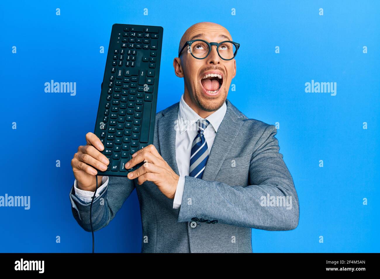 Bald man with beard holding keyboard angry and mad screaming frustrated ...
