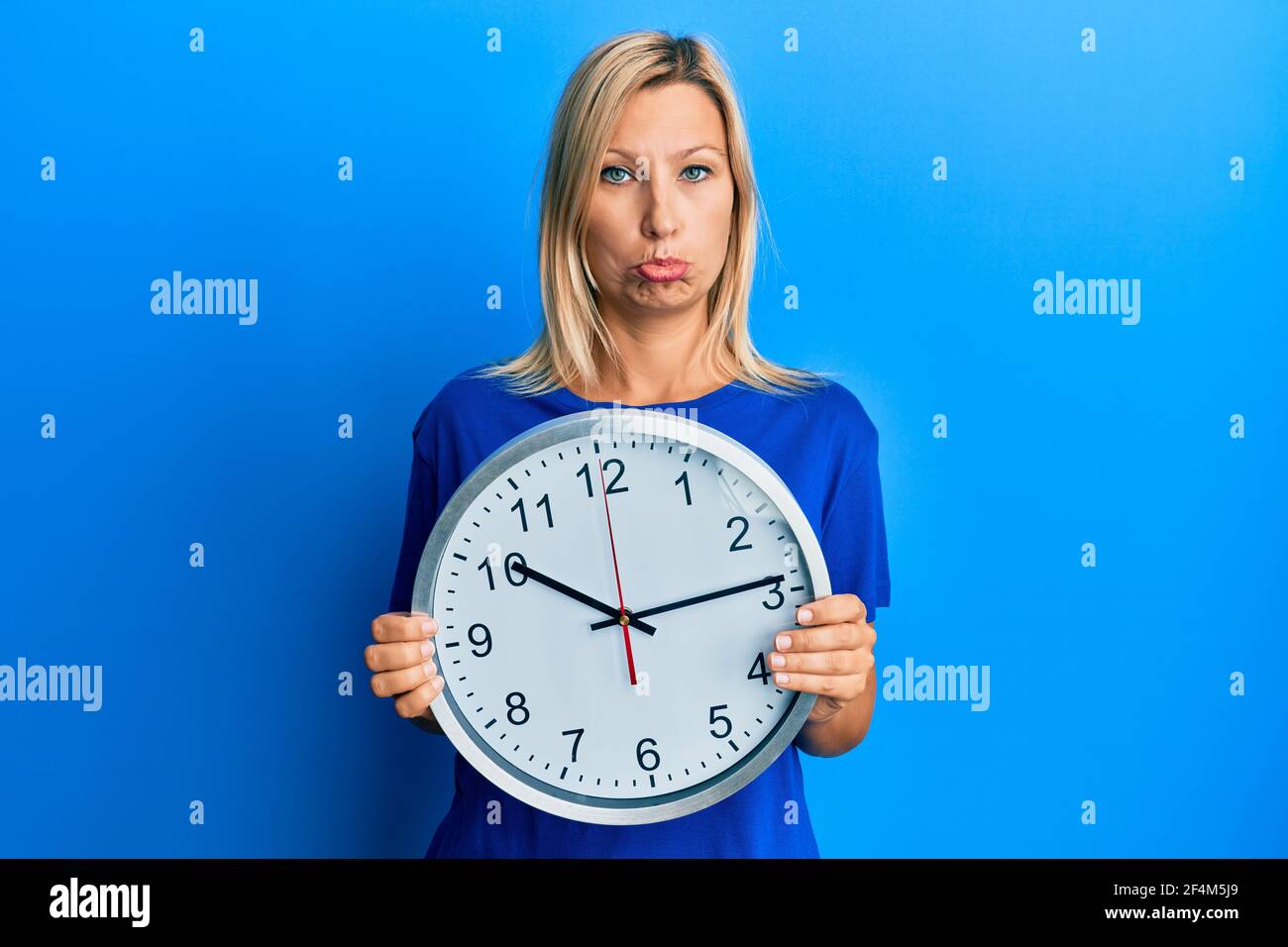 Beautiful middle age blonde woman holding big clock depressed and worry ...