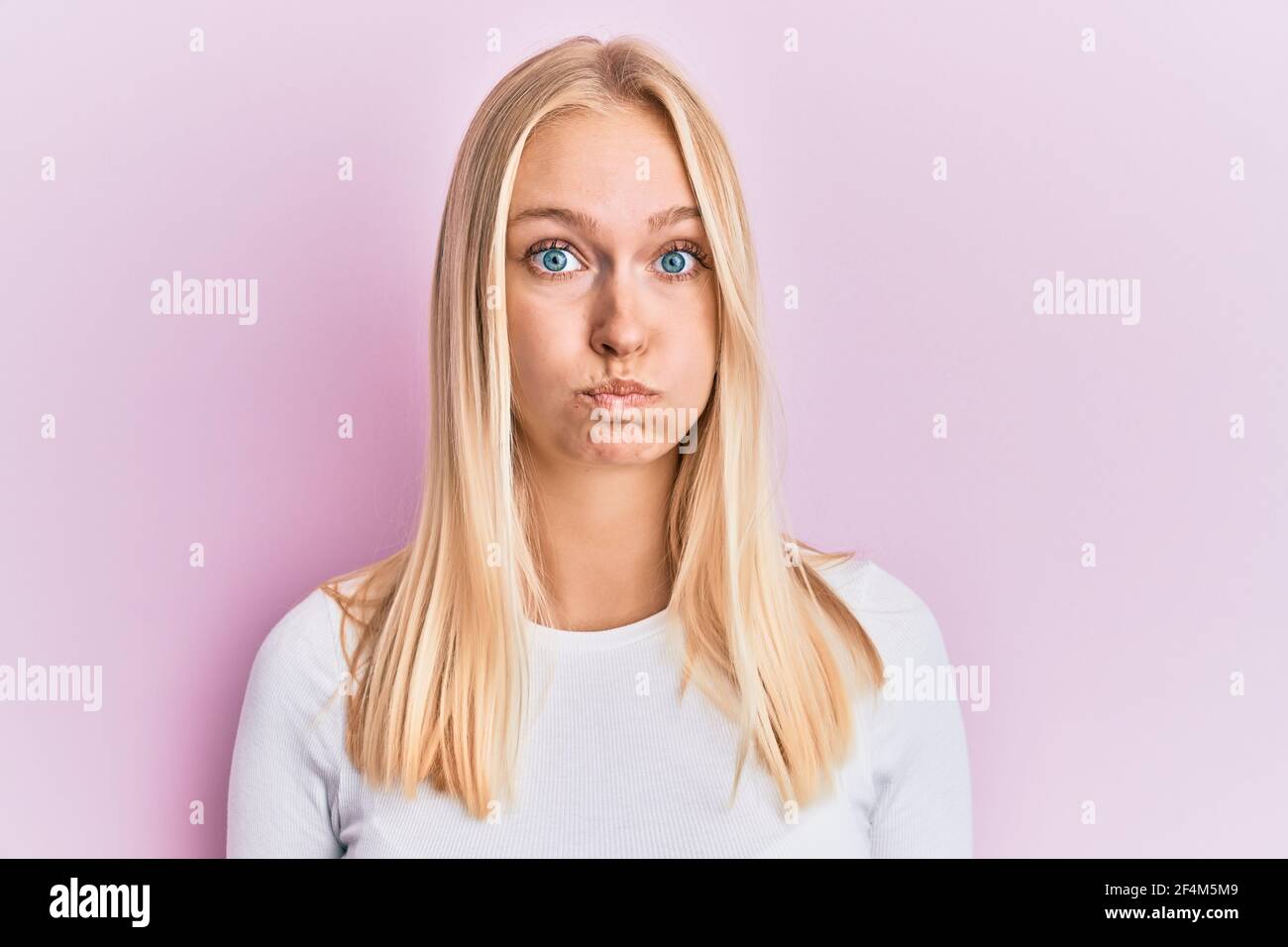 Young blonde girl wearing casual clothes puffing cheeks with funny face ...