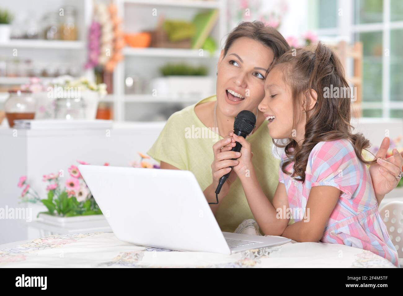 Mother and daughter sitting at table with laptop singing karaoke Stock ...