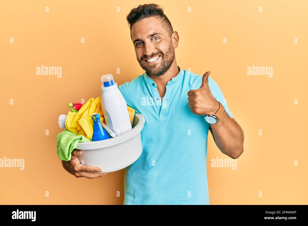 Handsome man with beard holding cleaning products smiling happy and ...
