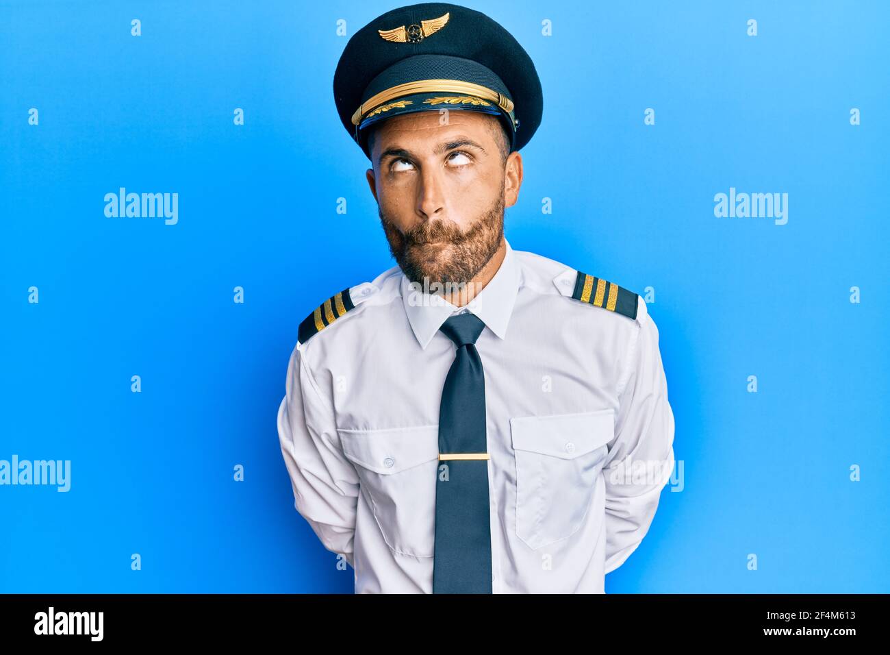 Handsome man with beard wearing airplane pilot uniform making fish face ...