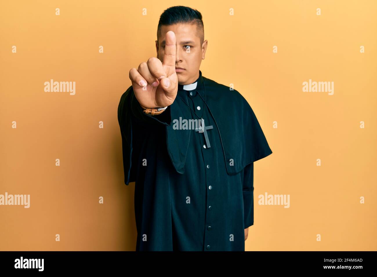 Young latin priest man standing over yellow background pointing with ...