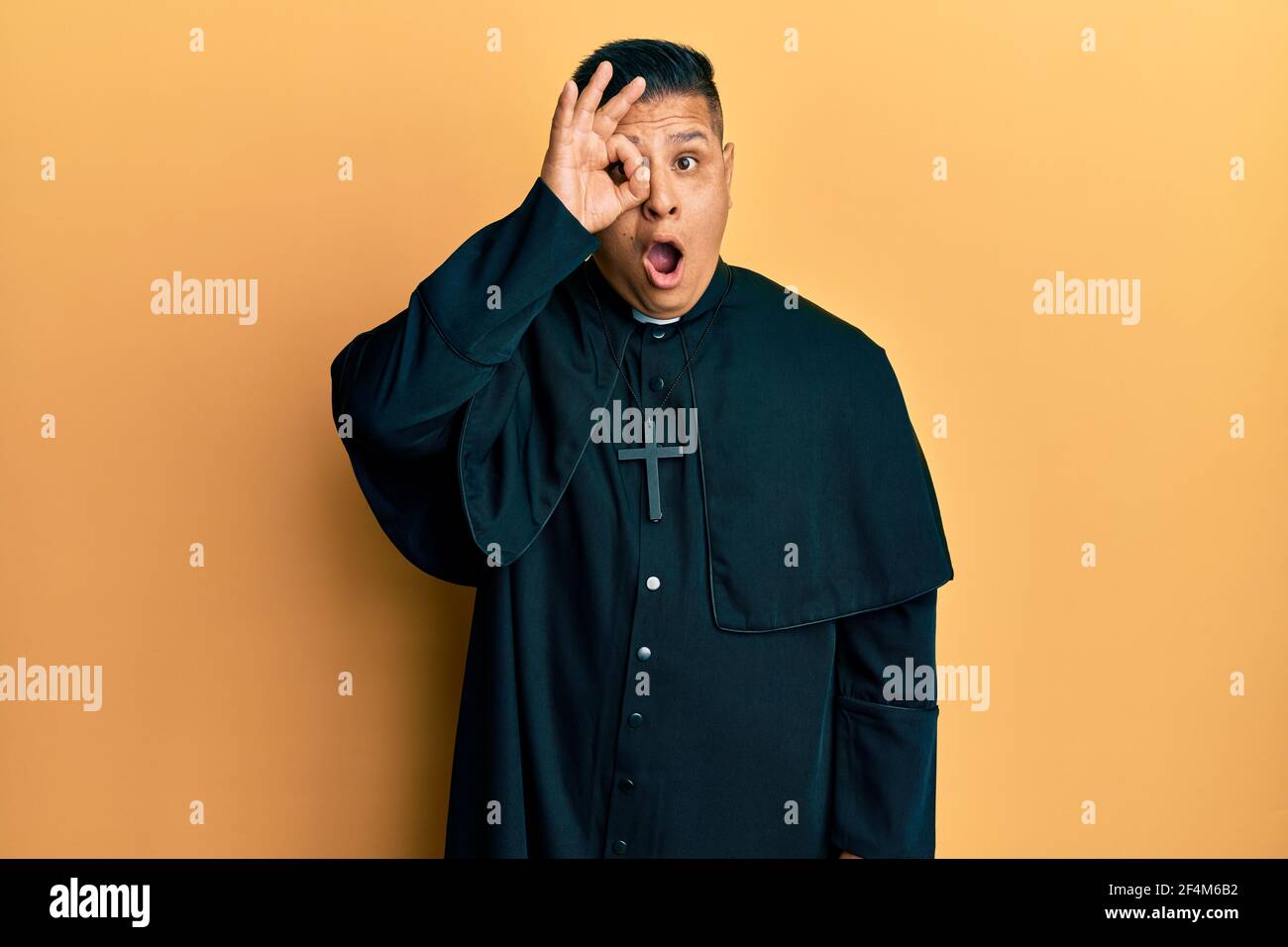 Young latin priest man standing over yellow background doing ok gesture ...