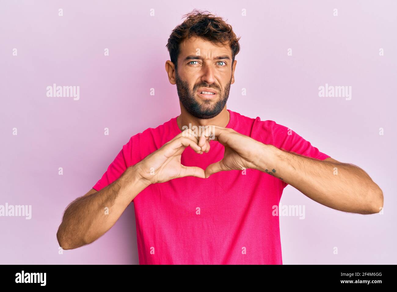 Handsome man with beard making heart symbol with hands shape clueless ...