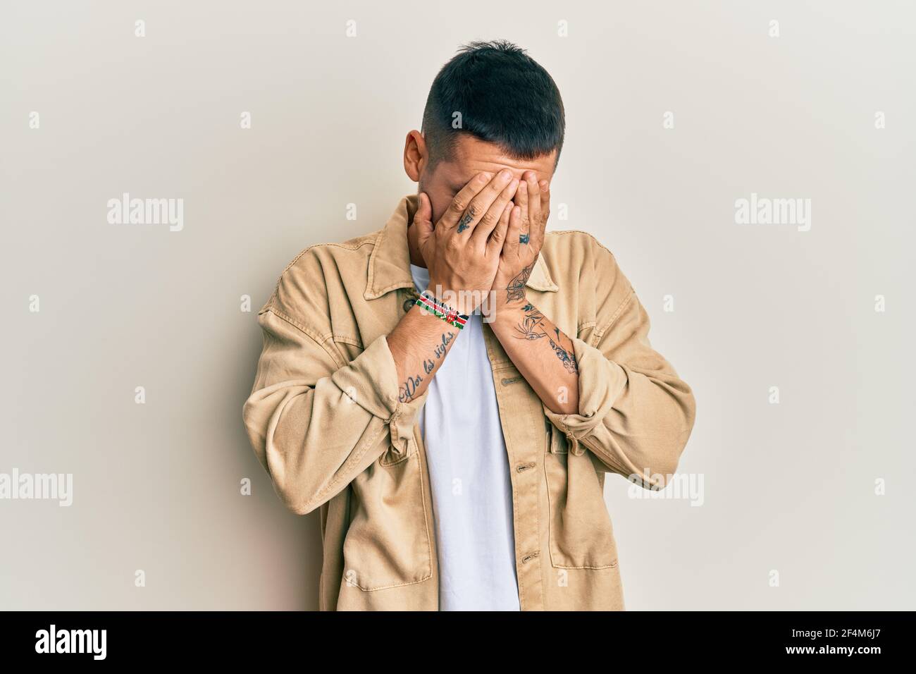 Handsome man with tattoos wearing casual brown denim jacket with sad ...