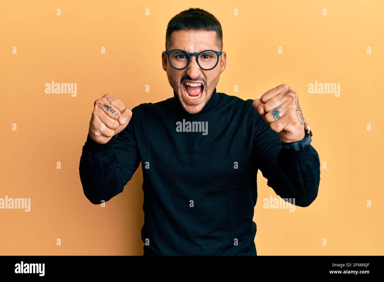 Handsome man with tattoos wearing turtleneck sweater and glasses angry ...