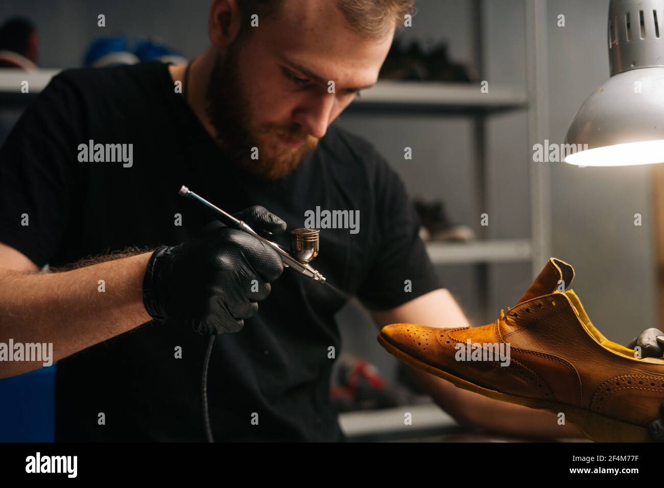 Portrait of bearded shoemaker wearing black gloves spraying paint of ...