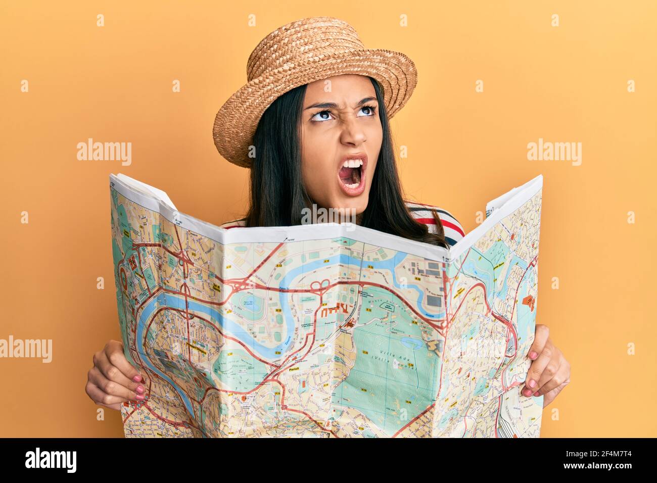 Young hispanic woman wearing summer hat holding map angry and mad ...