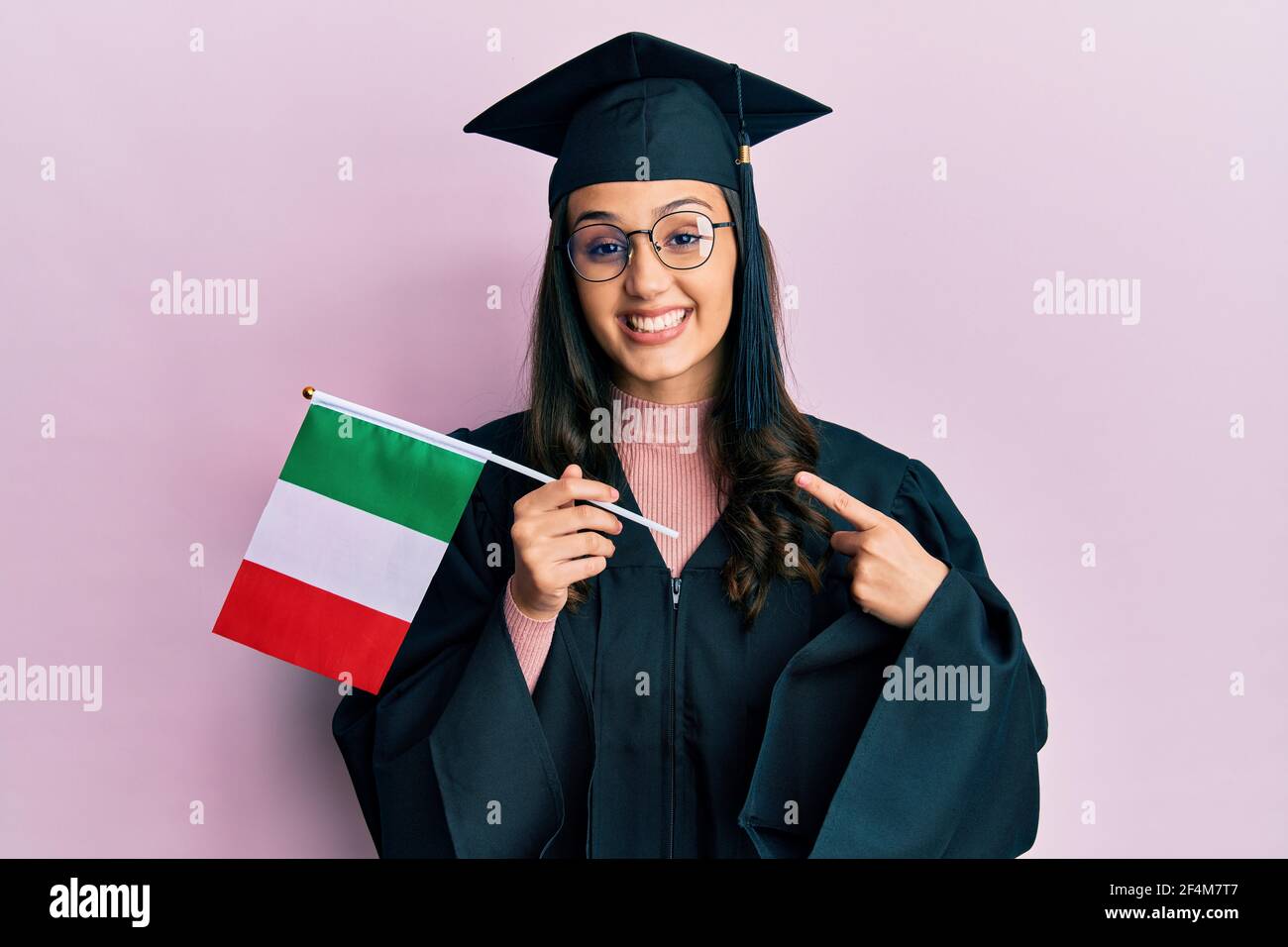 Young hispanic woman wearing graduation uniform holding italy flag ...
