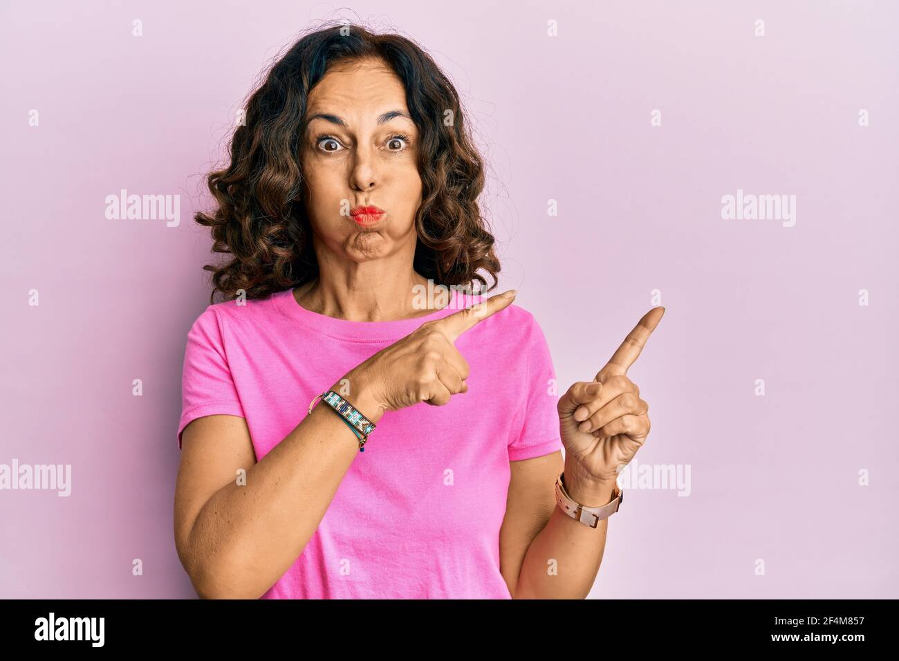 Middle age hispanic woman pointing with fingers to the side puffing ...