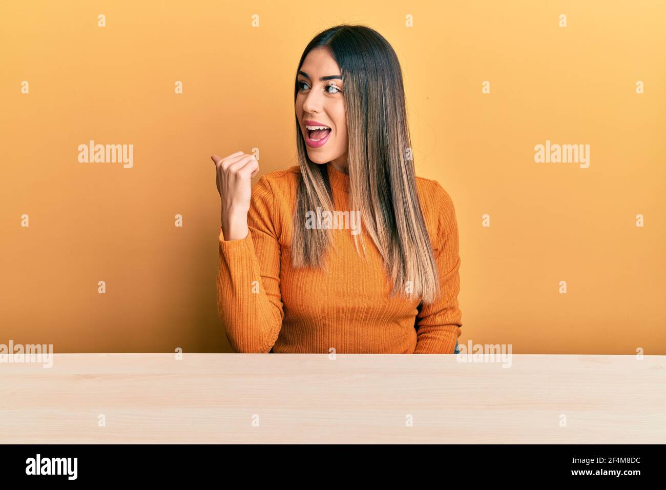 Young hispanic woman wearing casual clothes sitting on the table ...