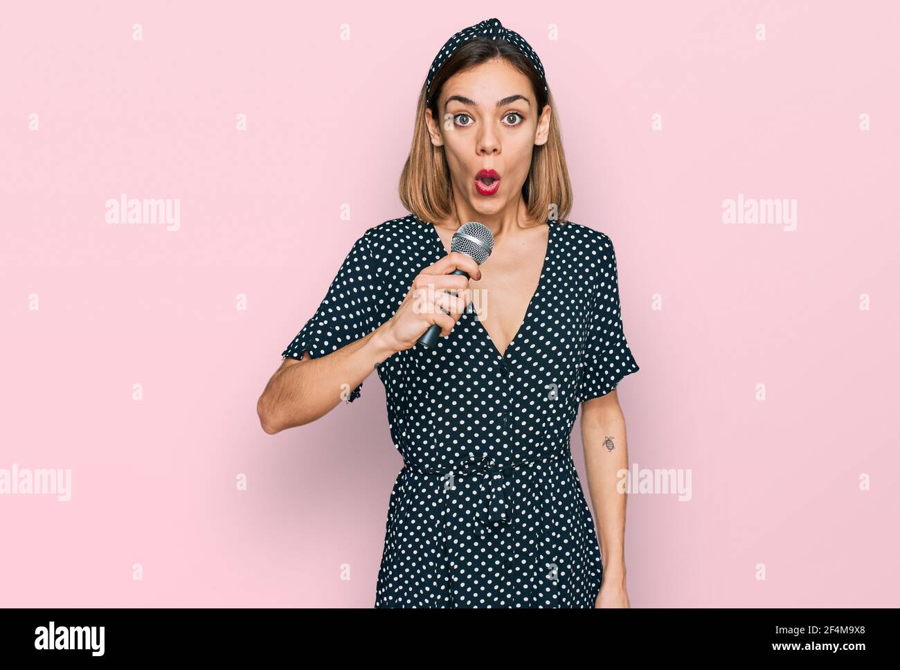 Young blonde girl singing song using microphone scared and amazed with ...