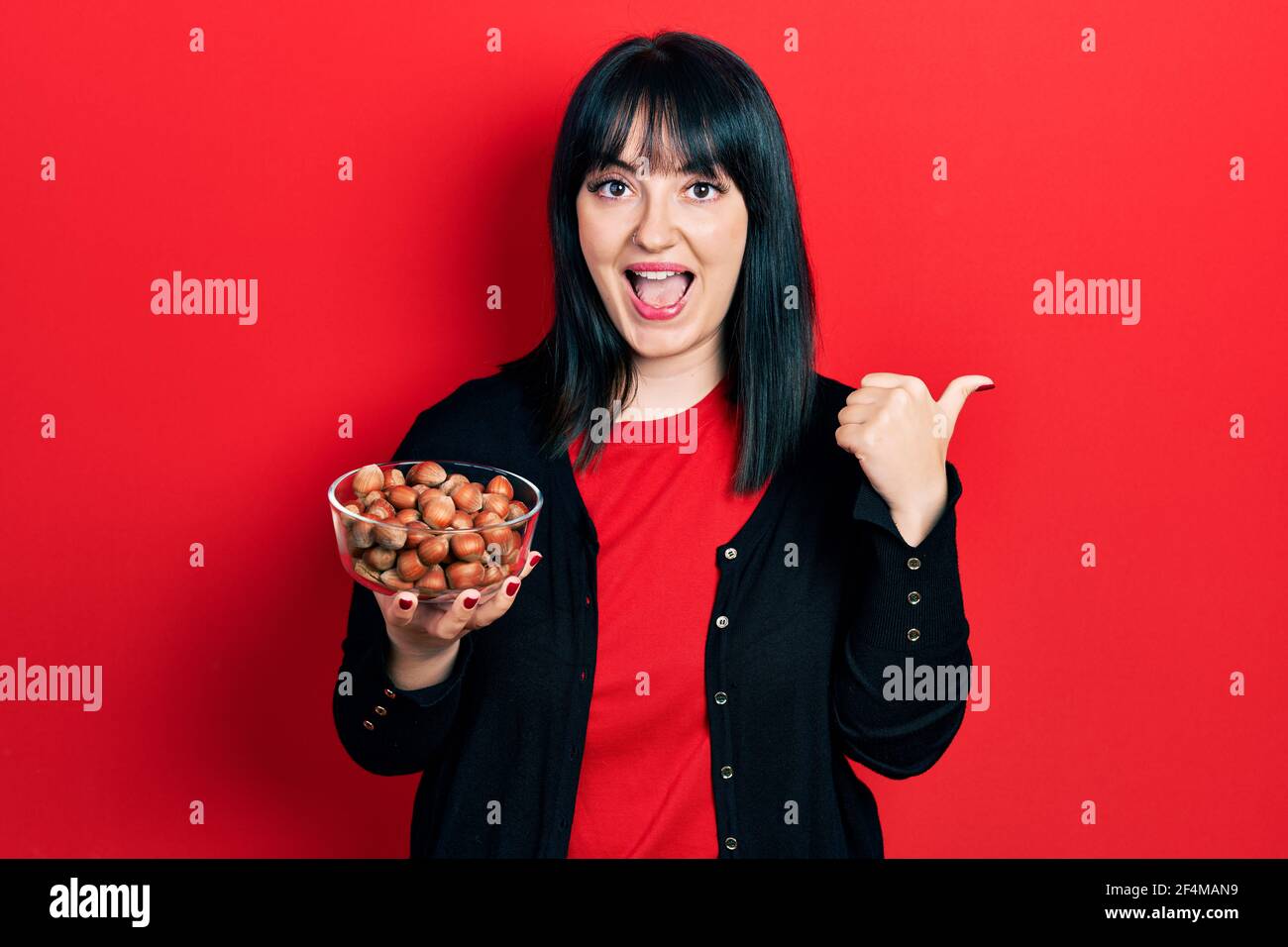 Young hispanic woman holding bowl of chestnuts pointing thumb up to the ...