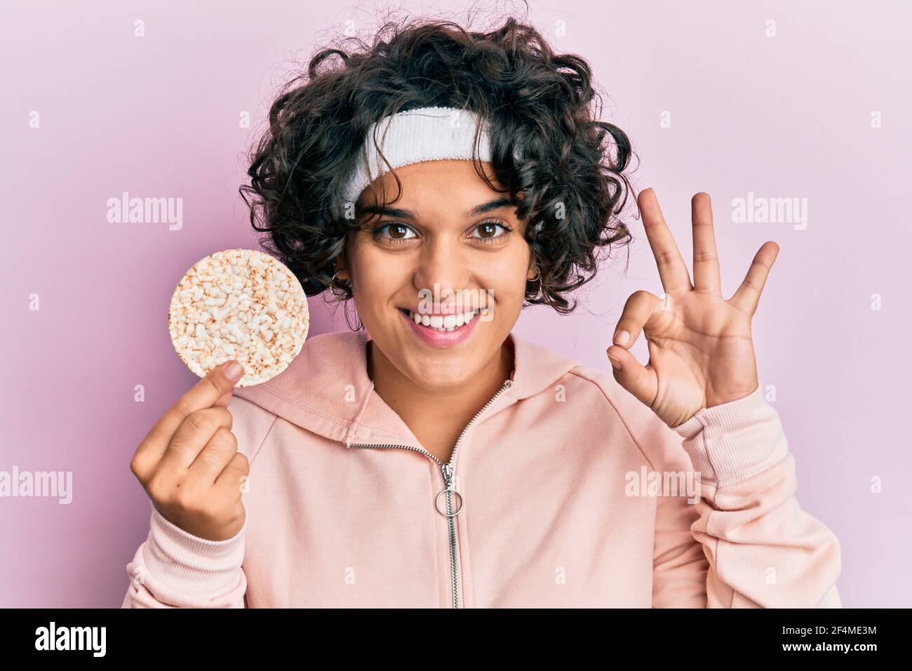 Young hispanic woman with curly hair eating healthy rice crackers doing ...