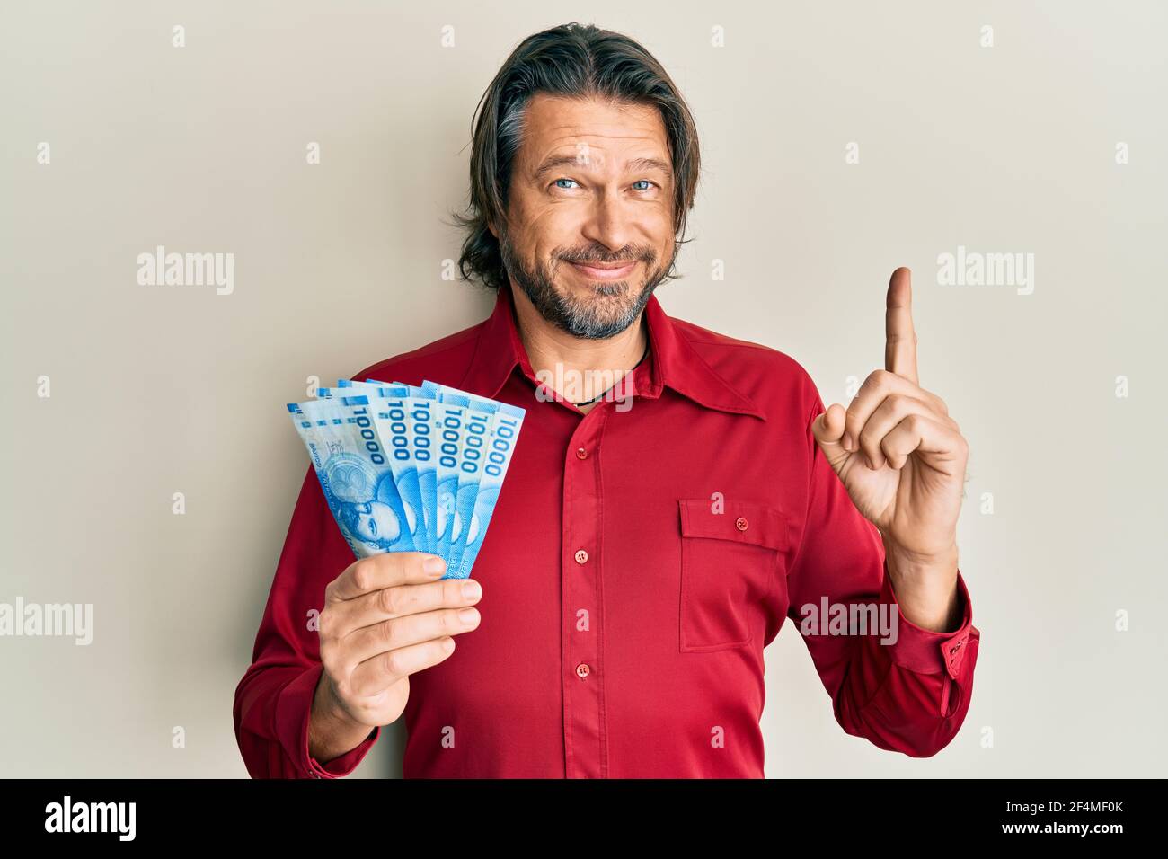 Middle age handsome man holding 10000 chilean pesos smiling with an ...