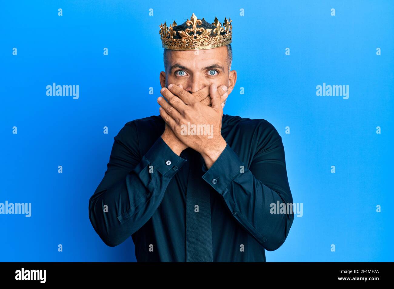 Middle age handsome business man wearing king crown shocked covering ...