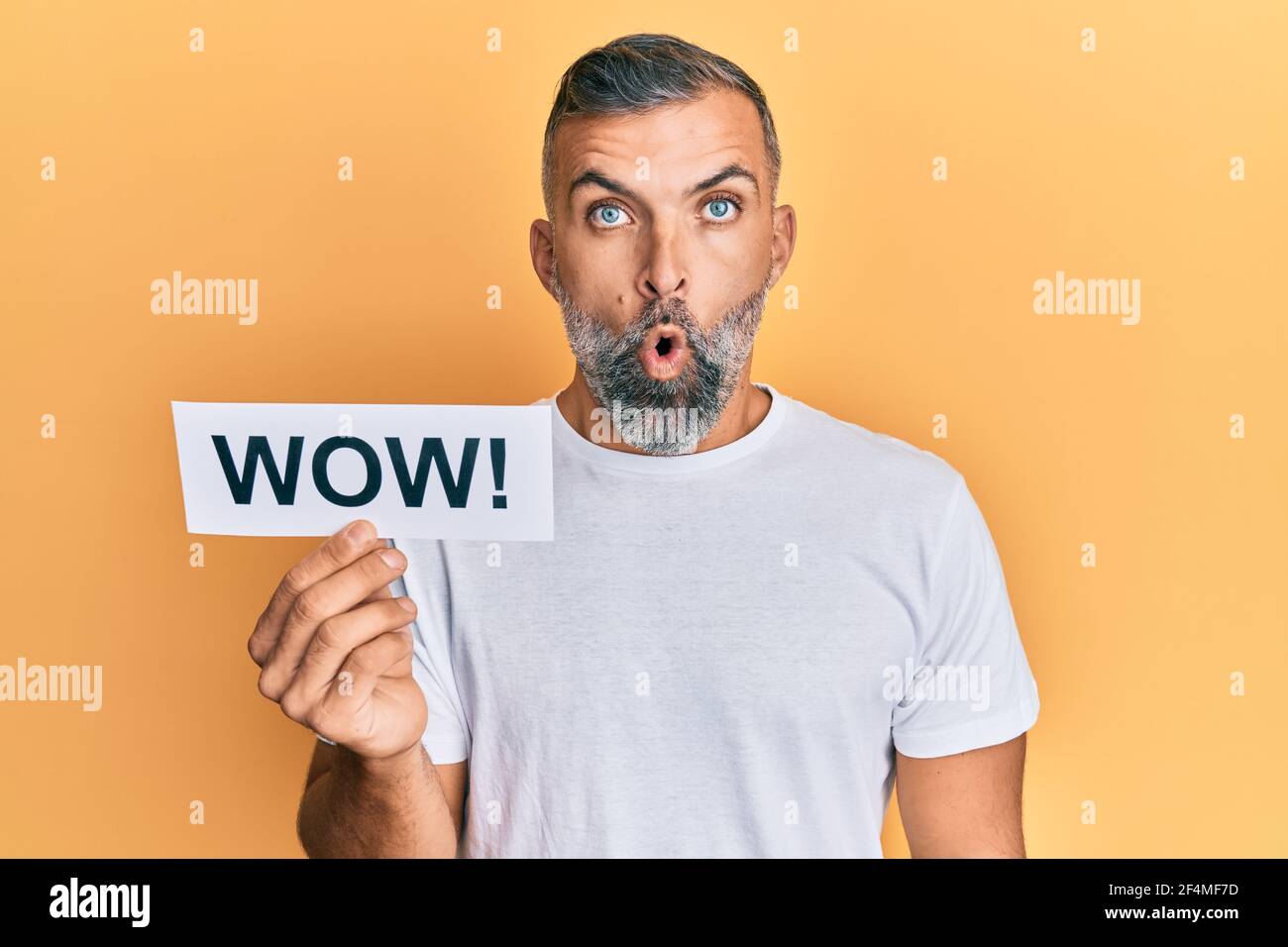 Middle age handsome man holding wow word on paper scared and amazed ...
