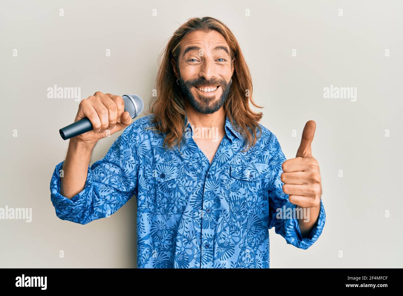 Attractive man with long hair and beard singing song using microphone ...