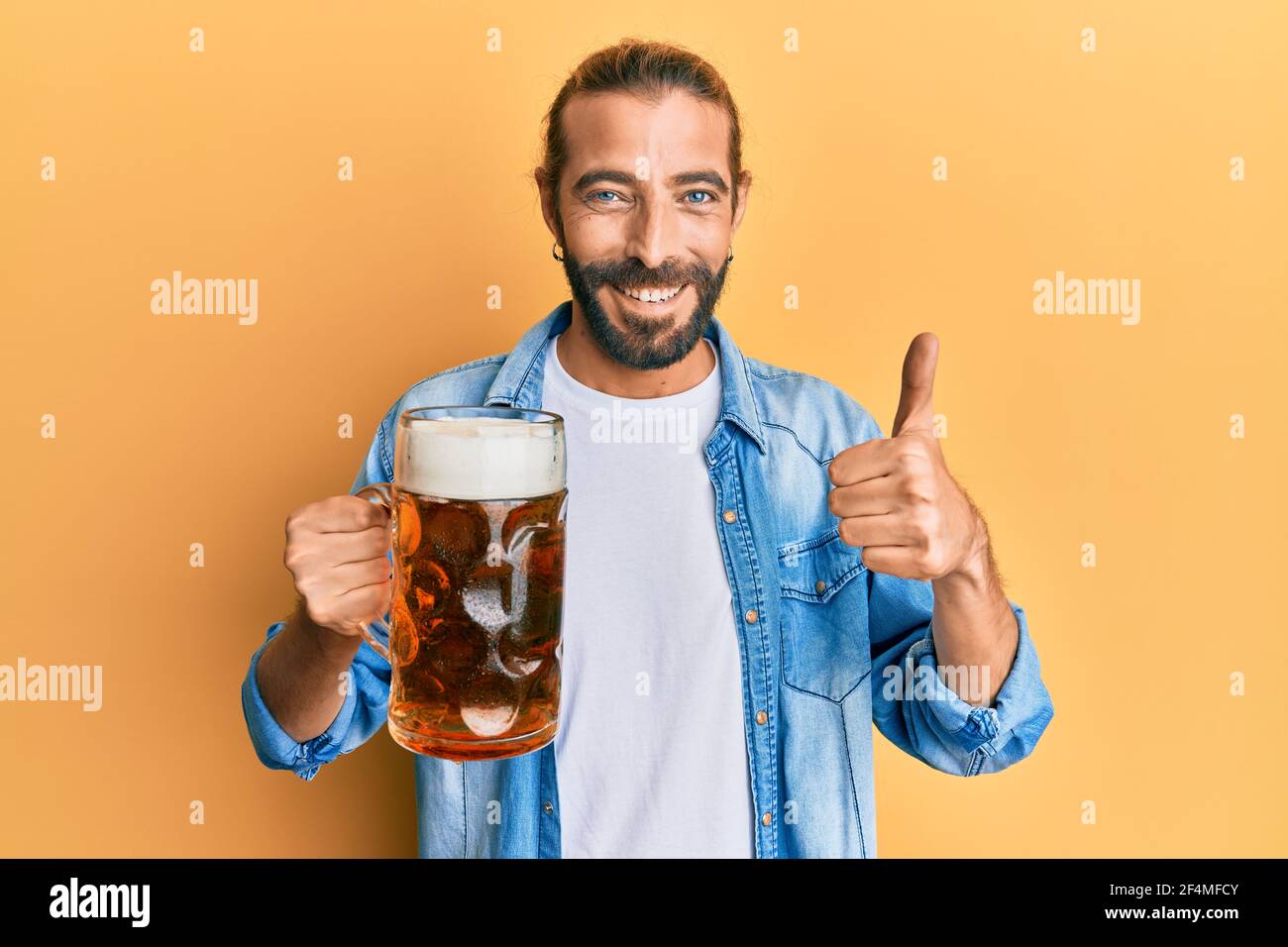 Attractive man with long hair and beard drinking a pint of beer smiling ...