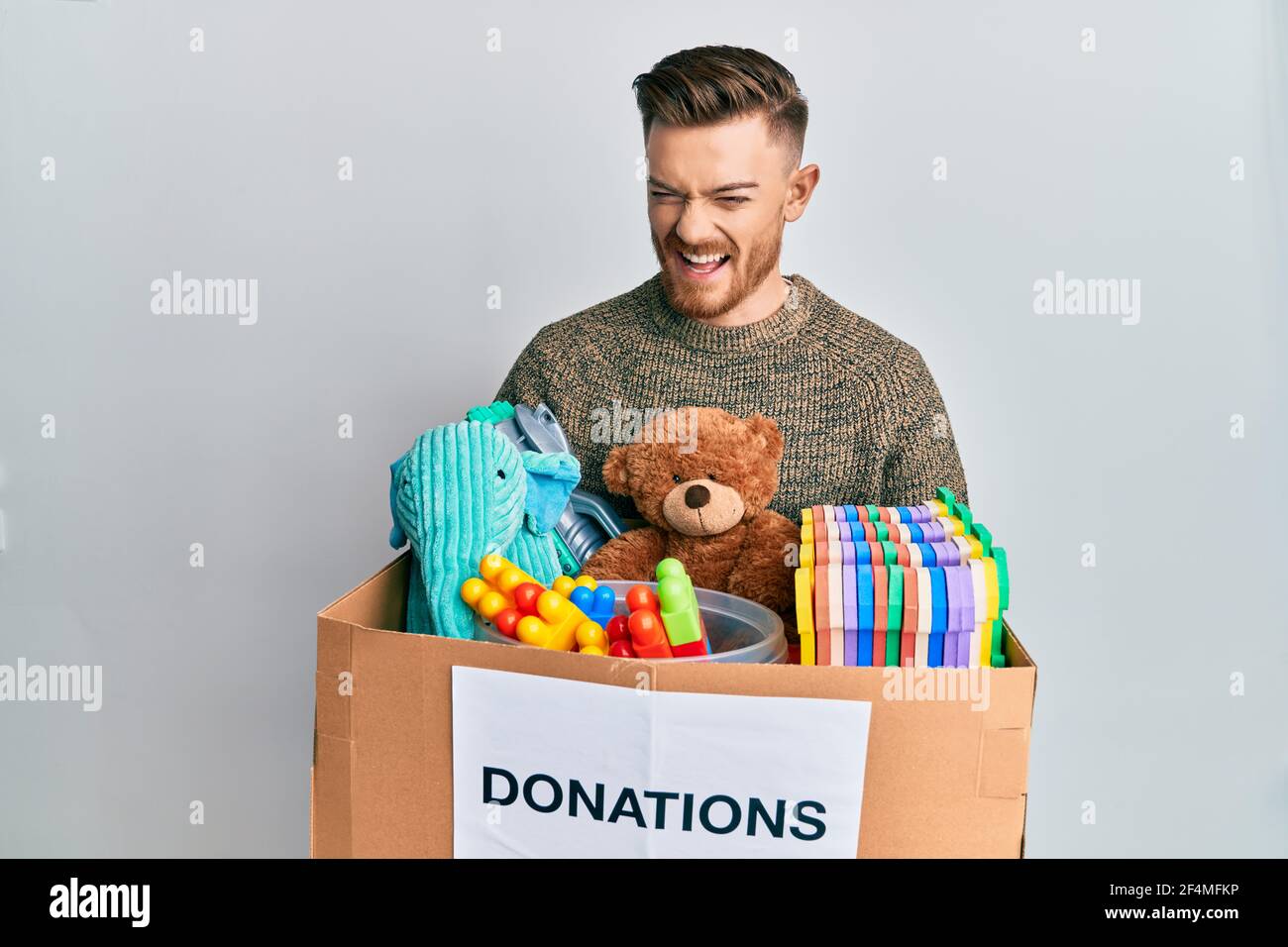 Young redhead man holding donation box with toys smiling and laughing ...