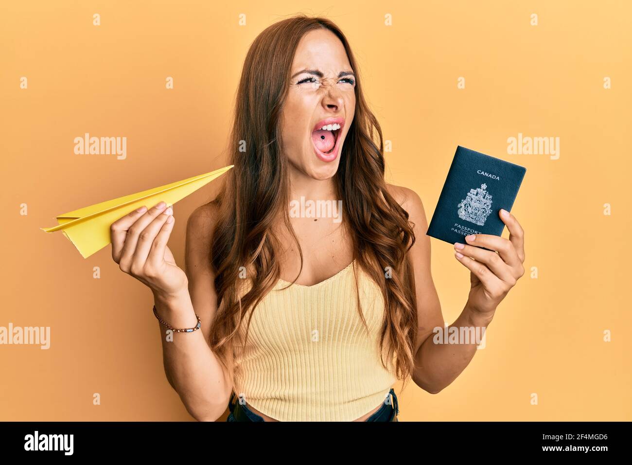 Young brunette woman holding paper airplane and canadian passport angry ...