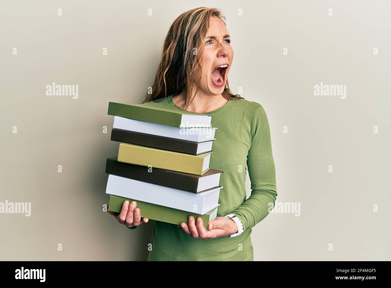 Young blonde woman holding a pile of books angry and mad screaming ...