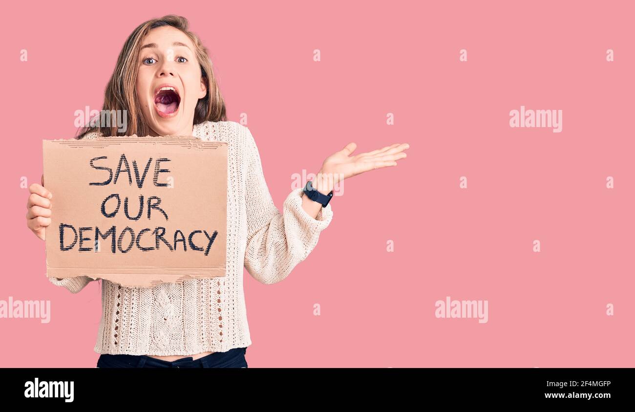 Young beautiful blonde woman holding save our democracy banner ...