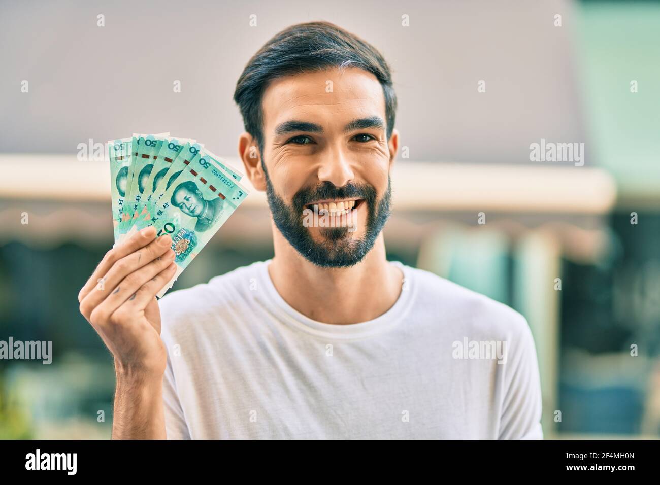 Young hispanic man smiling happy holding chinese yuan banknotes at the ...