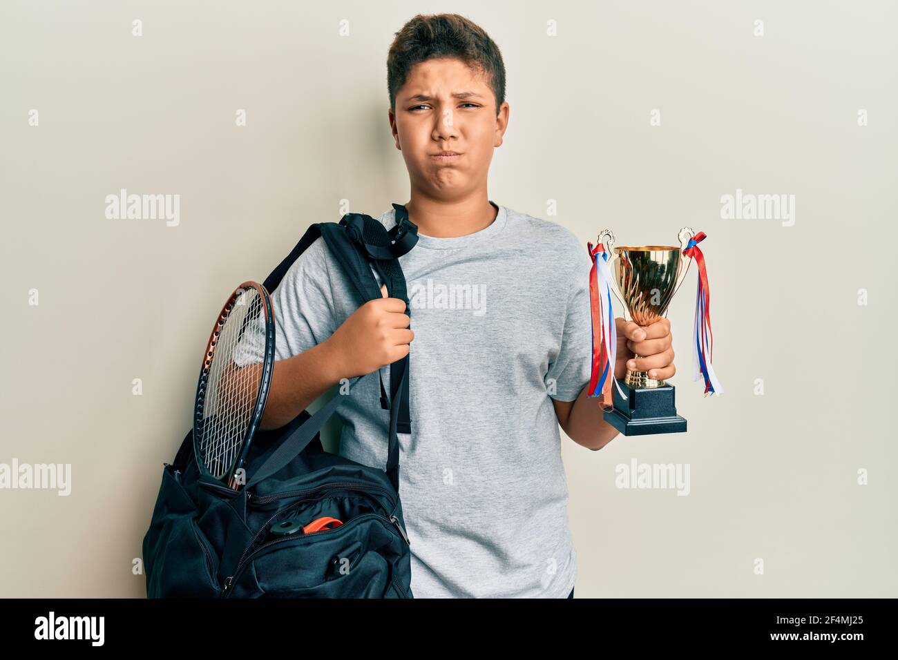 Teenager hispanic boy holding sport bag holding trophy puffing cheeks ...