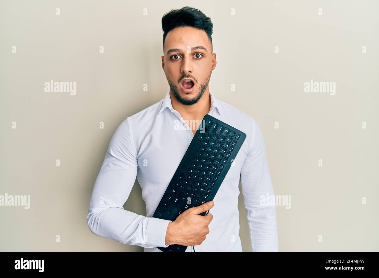Young arab man holding computer keyboard scared and amazed with open ...