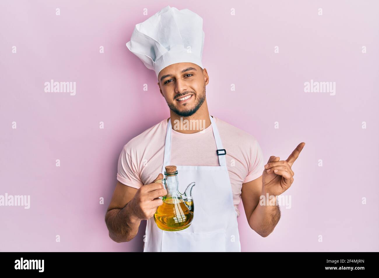 Young arab man wearing professional cook uniform holding olive oil can ...