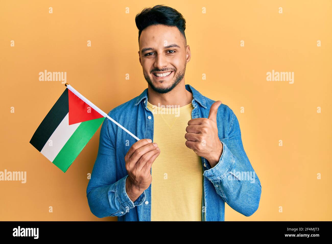 Young arab man holding palestine flag smiling happy and positive, thumb ...