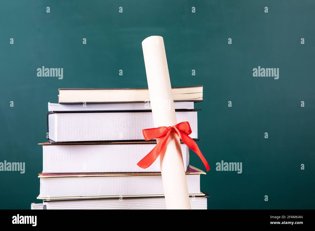 Diploma with a red ribbon and a stack of books on green chalkboard ...