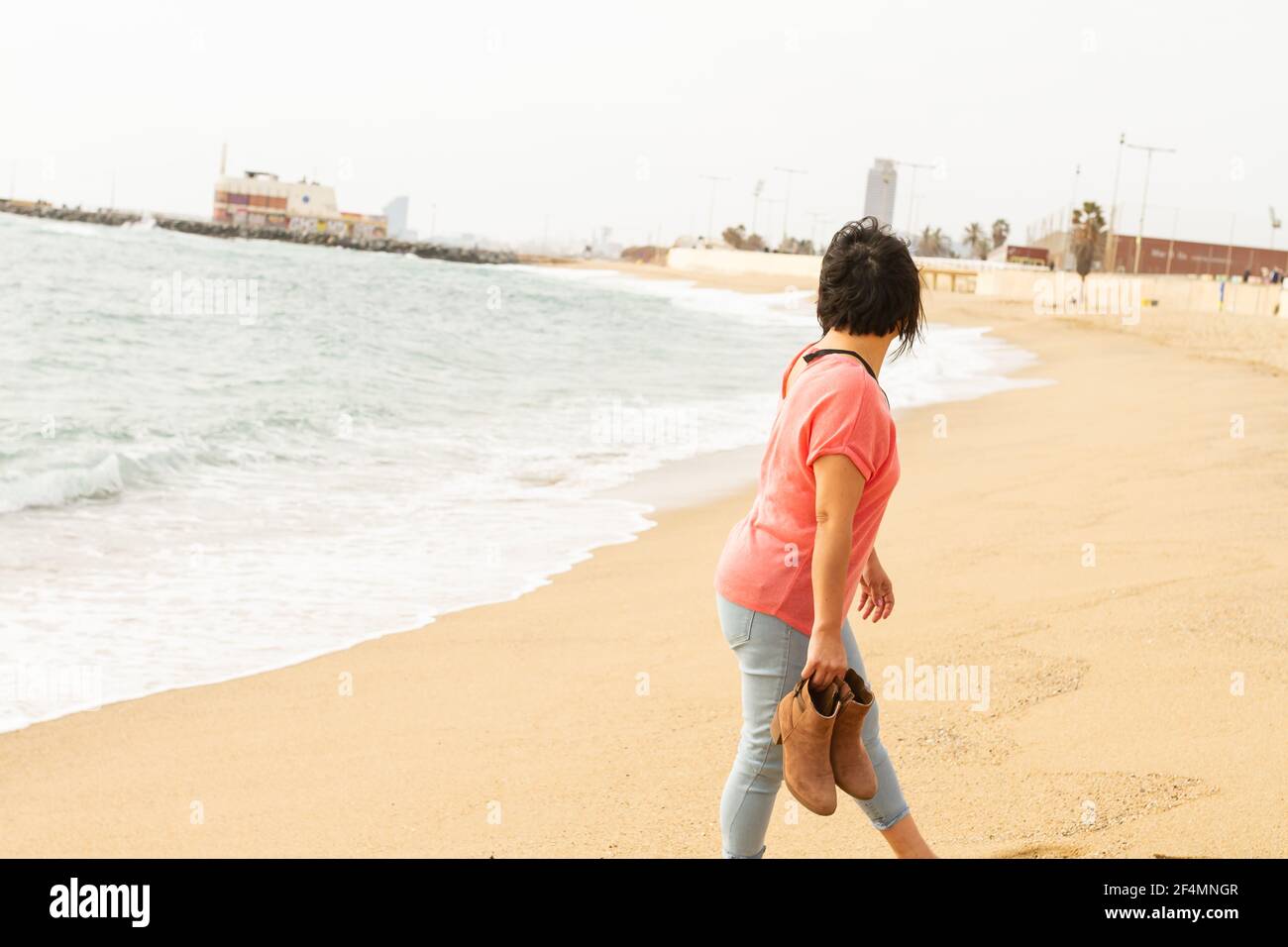 Scenic shot of a Hispanic woman walking on the sand in Barceloneta ...