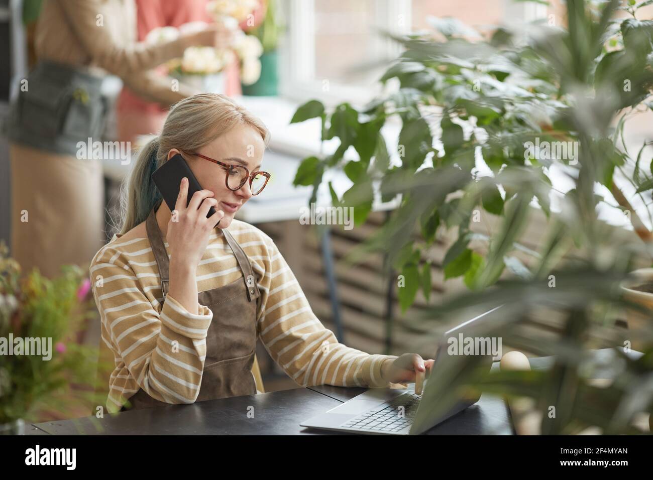 Side view portrait of young businesswoman speaking by phone in flower ...