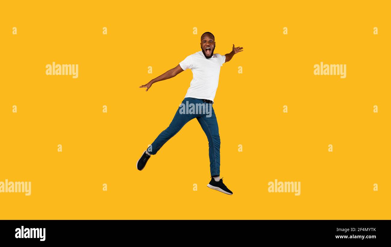 African Guy Jumping Shouting Looking At Camera, Yellow Background, Full ...