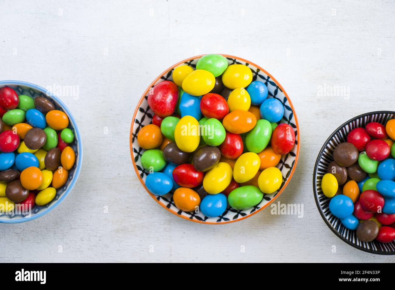 Top view of colorful chocolate candy balls in bowls on the white ...
